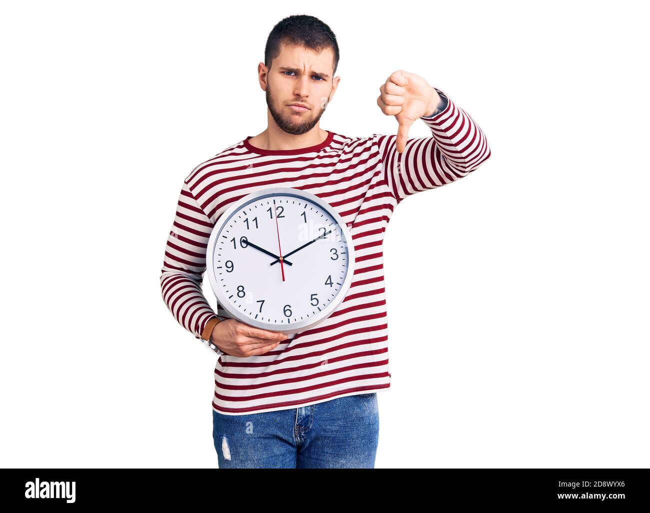 Young handsome man holding big clock with angry face, negative sign ...