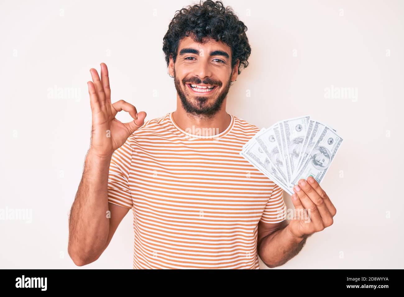 Handsome young man with curly hair and bear holding money bag with ...