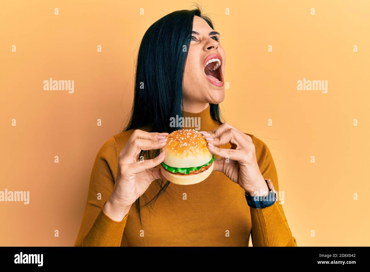 Young caucasian woman eating a tasty classic burger angry and mad ...