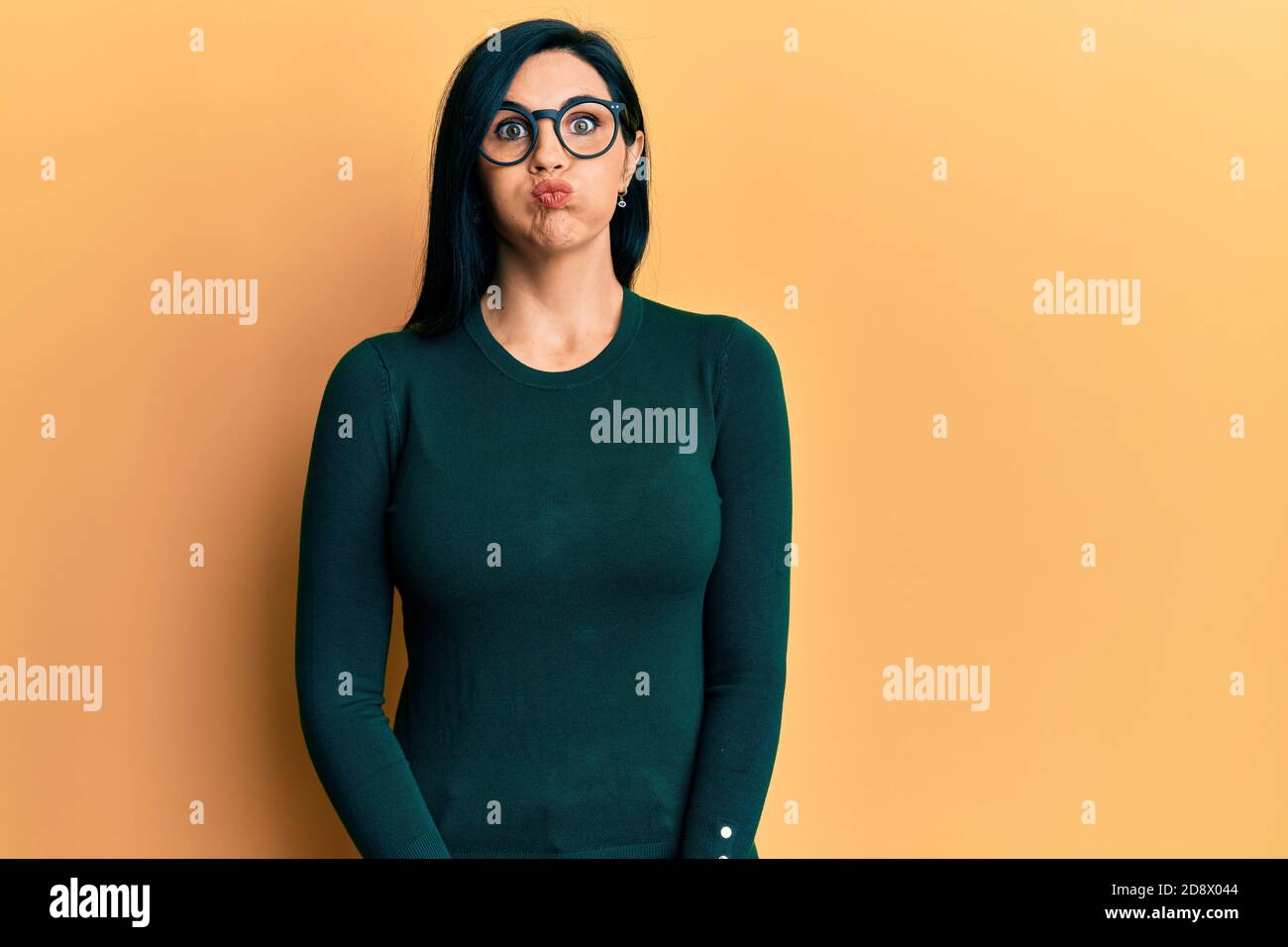 Young caucasian woman wearing casual clothes and glasses puffing cheeks ...