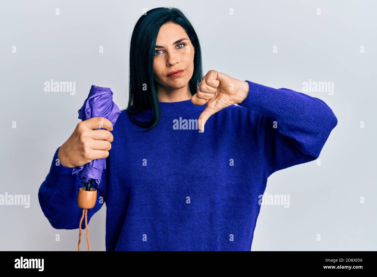 Young caucasian woman holding purple closed umbrella with angry face ...