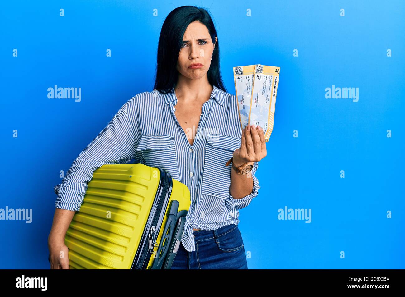 Young caucasian woman holding cabin suitcase and boarding tickets ...