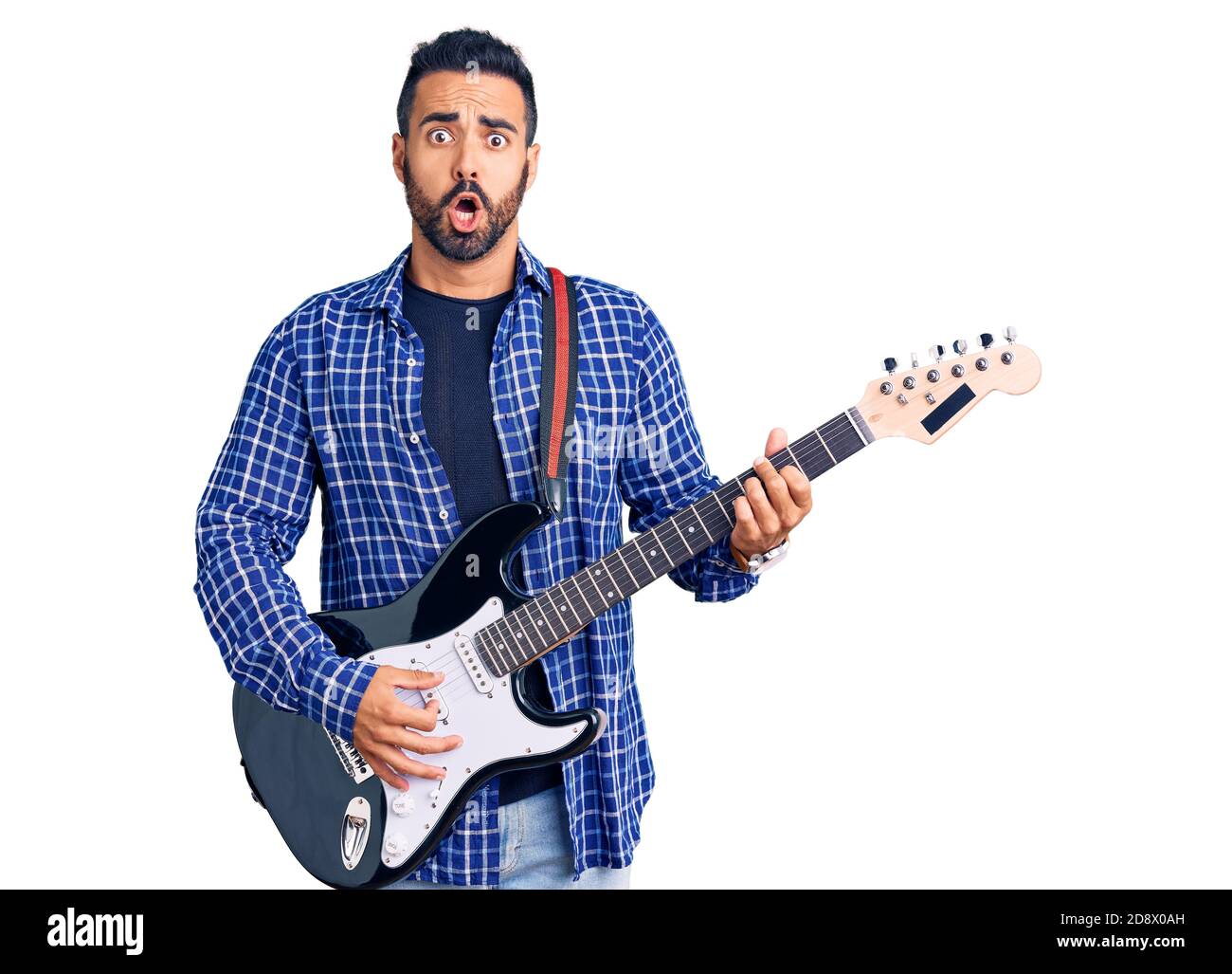 Young hispanic man playing electric guitar scared and amazed with open ...