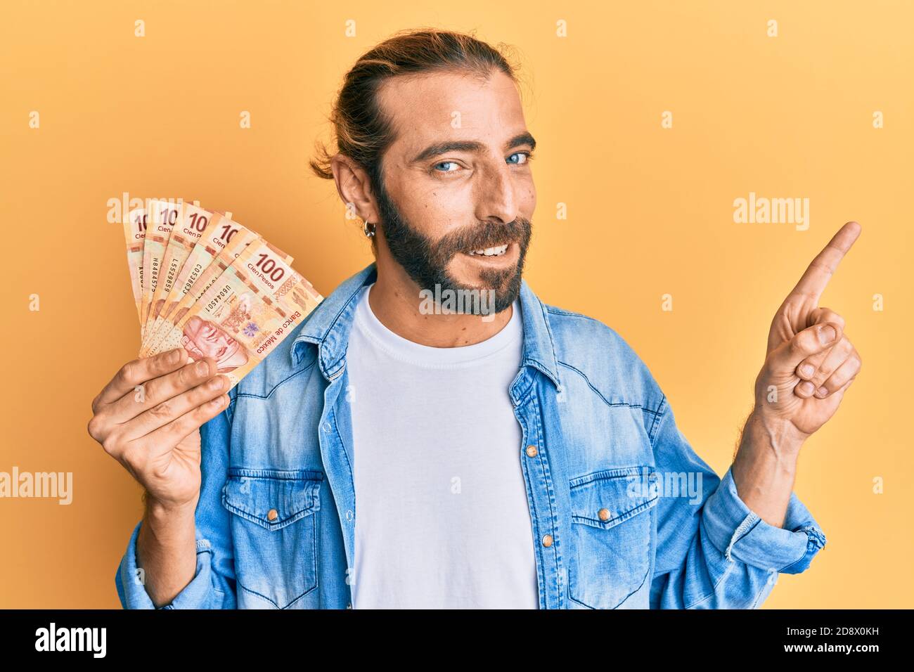 Attractive man with long hair and beard holding 100 mexican pesos ...
