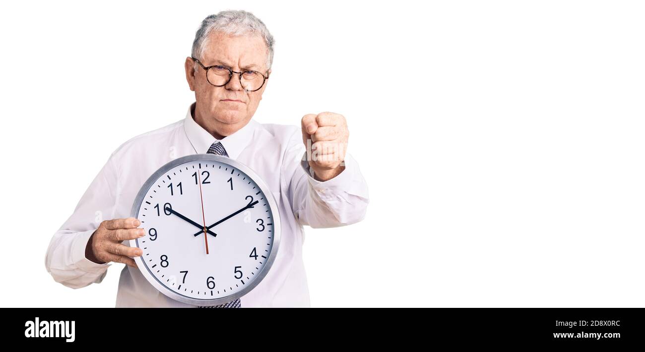 Senior grey-haired man wearing business clothes and holding clock ...