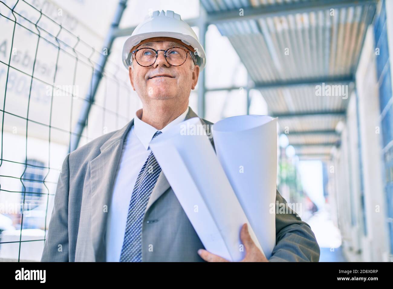 Senior grey-haired architect man holding blueprints walking at street ...