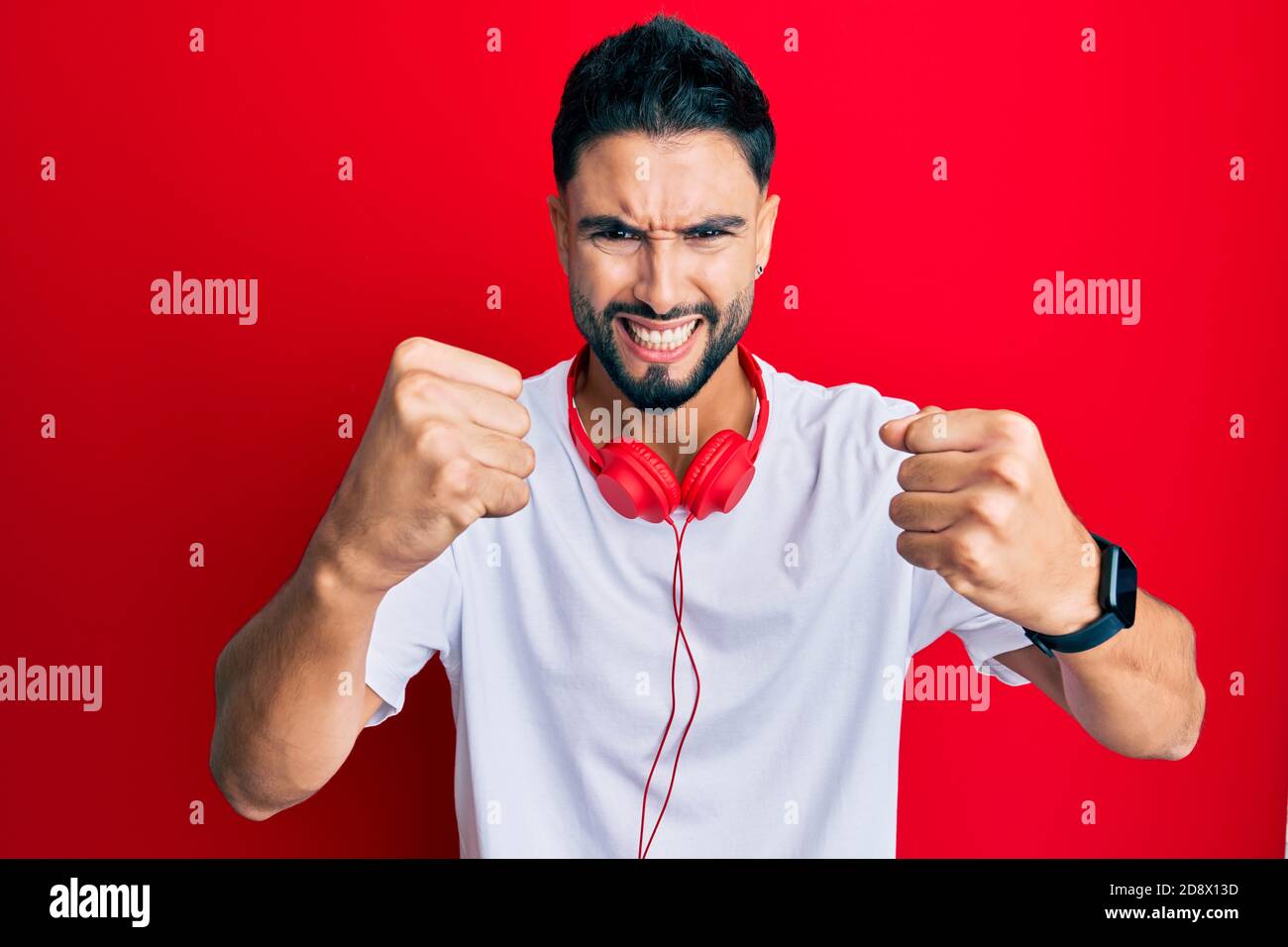 Young man with beard listening to music using headphones angry and mad ...