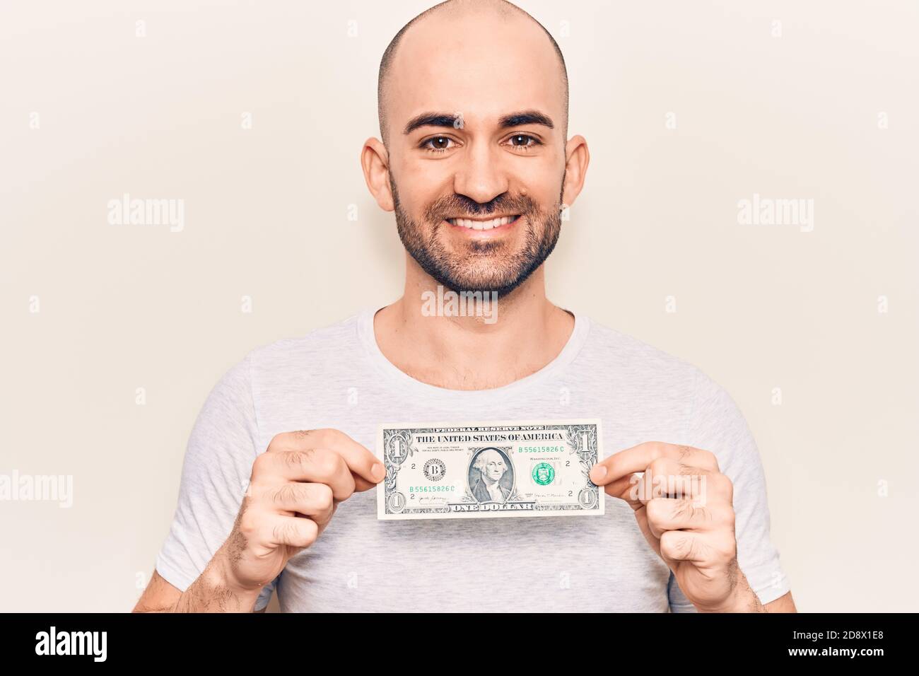 Young handsome bald man holding one dollar banknote looking positive ...