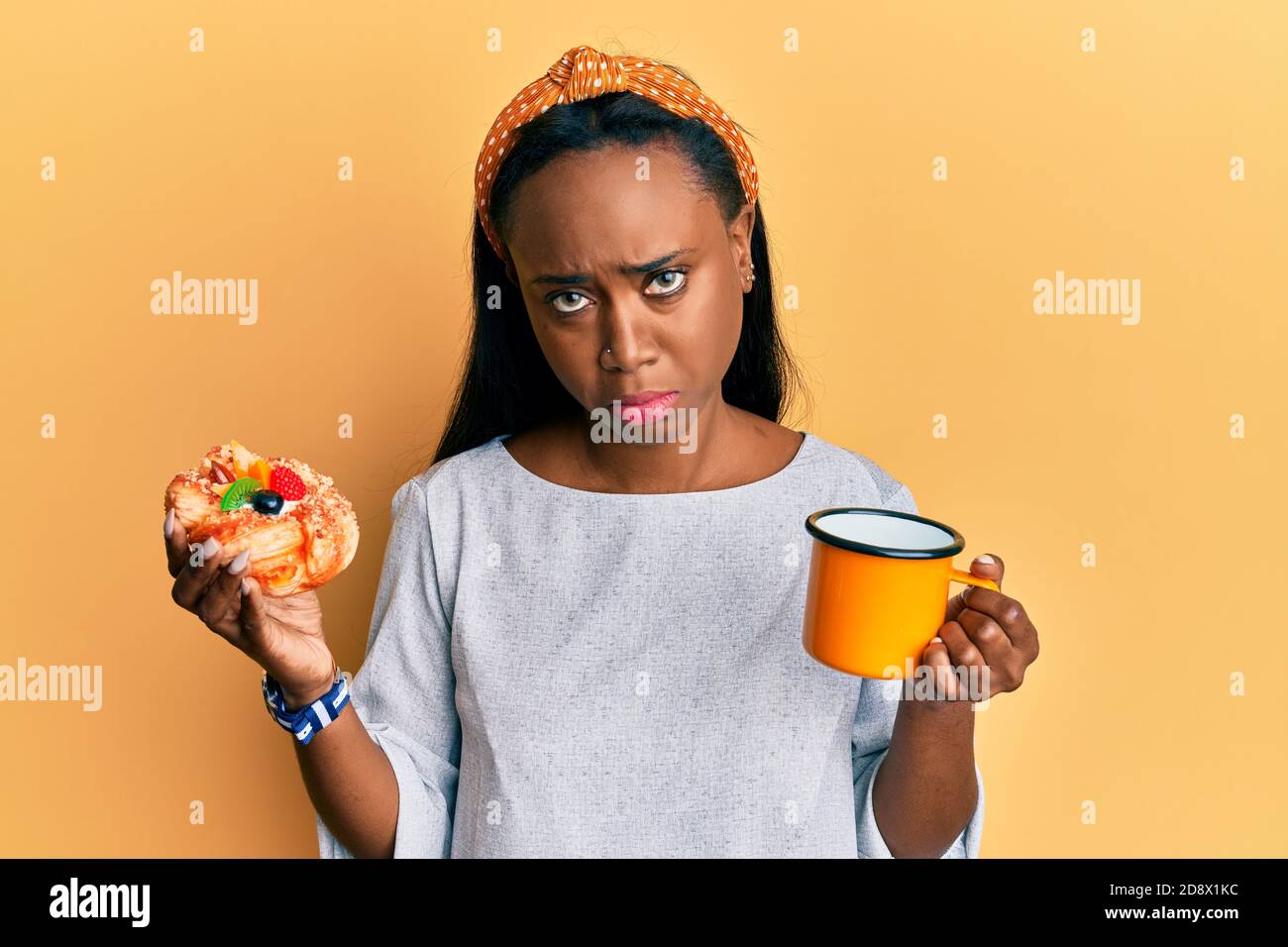 Young african woman drinking coffee and eating pastry depressed and ...
