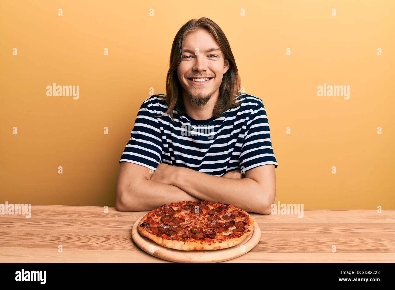 Handsome caucasian man with long hair eating tasty pepperoni pizza happy face smiling with ...