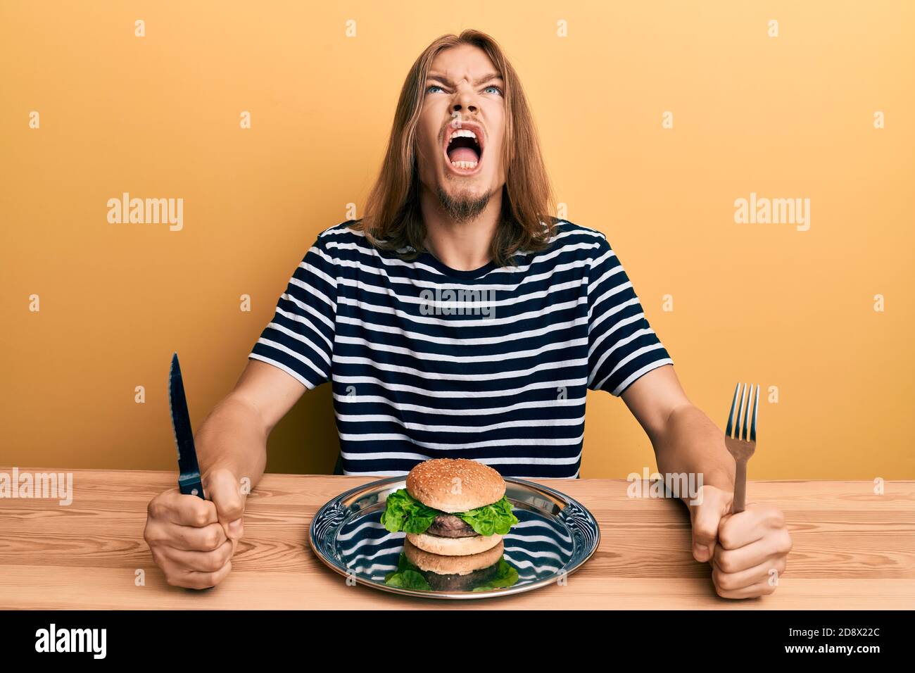 Handsome caucasian man with long hair eating a tasty classic burger ...
