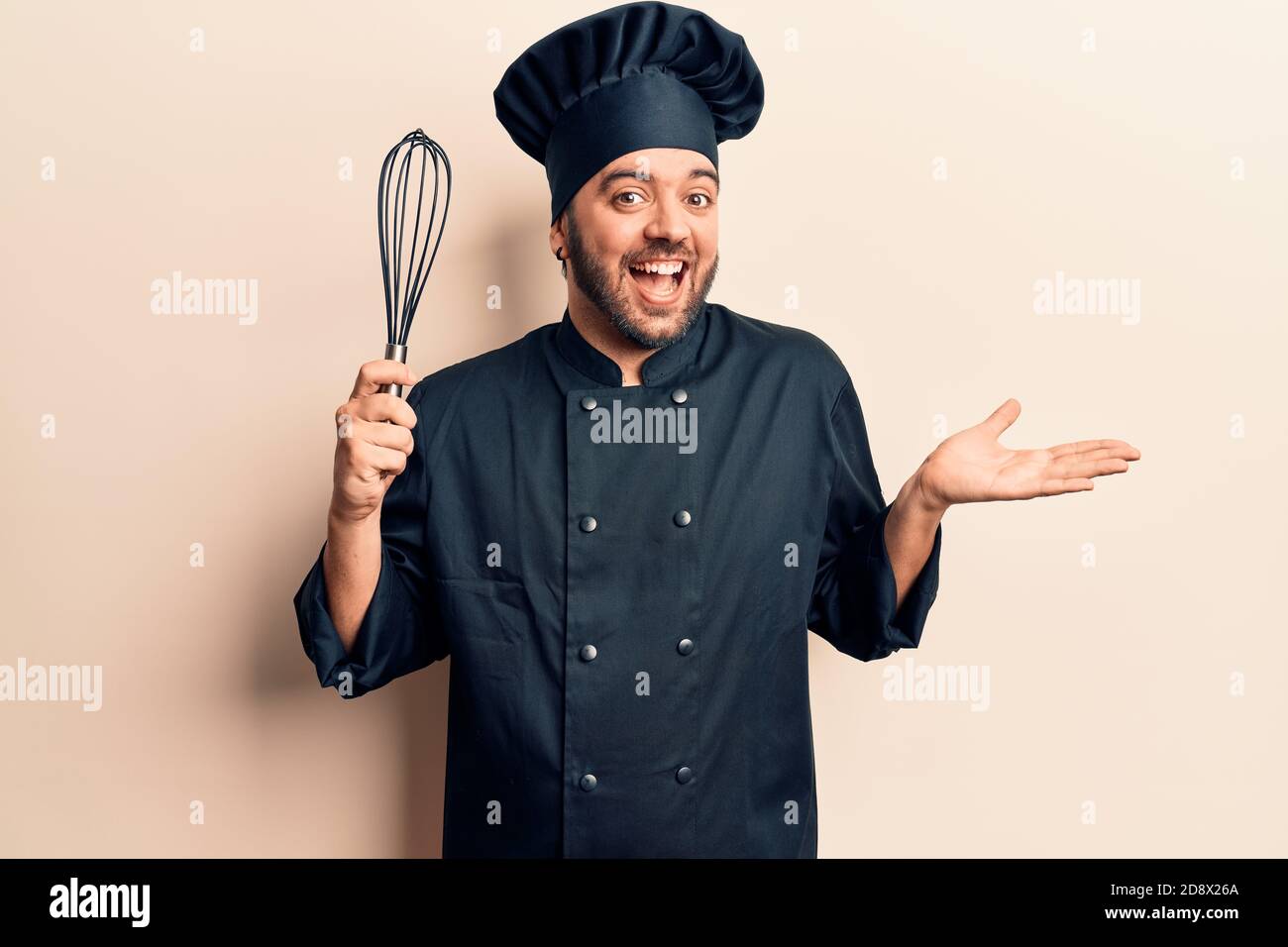 Young hispanic man wearing cooker uniform holding whisk celebrating ...