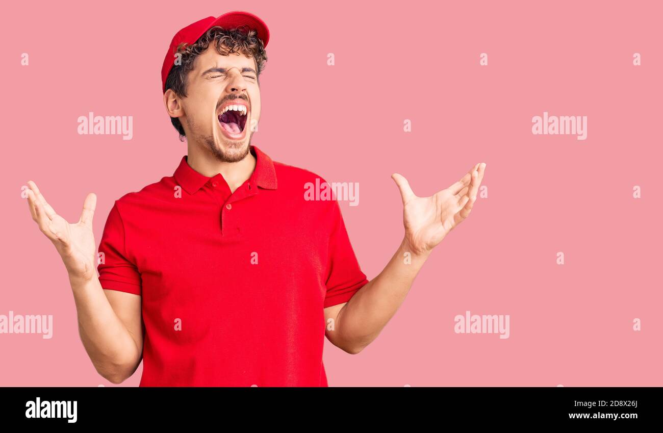 Young handsome man with curly hair wearing delivery uniform crazy and ...