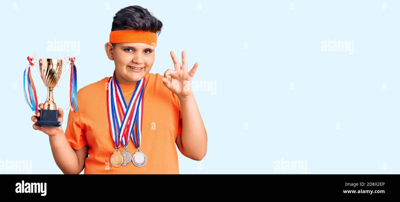 Little boy kid holding champion trophy and wearing medals doing ok sign ...