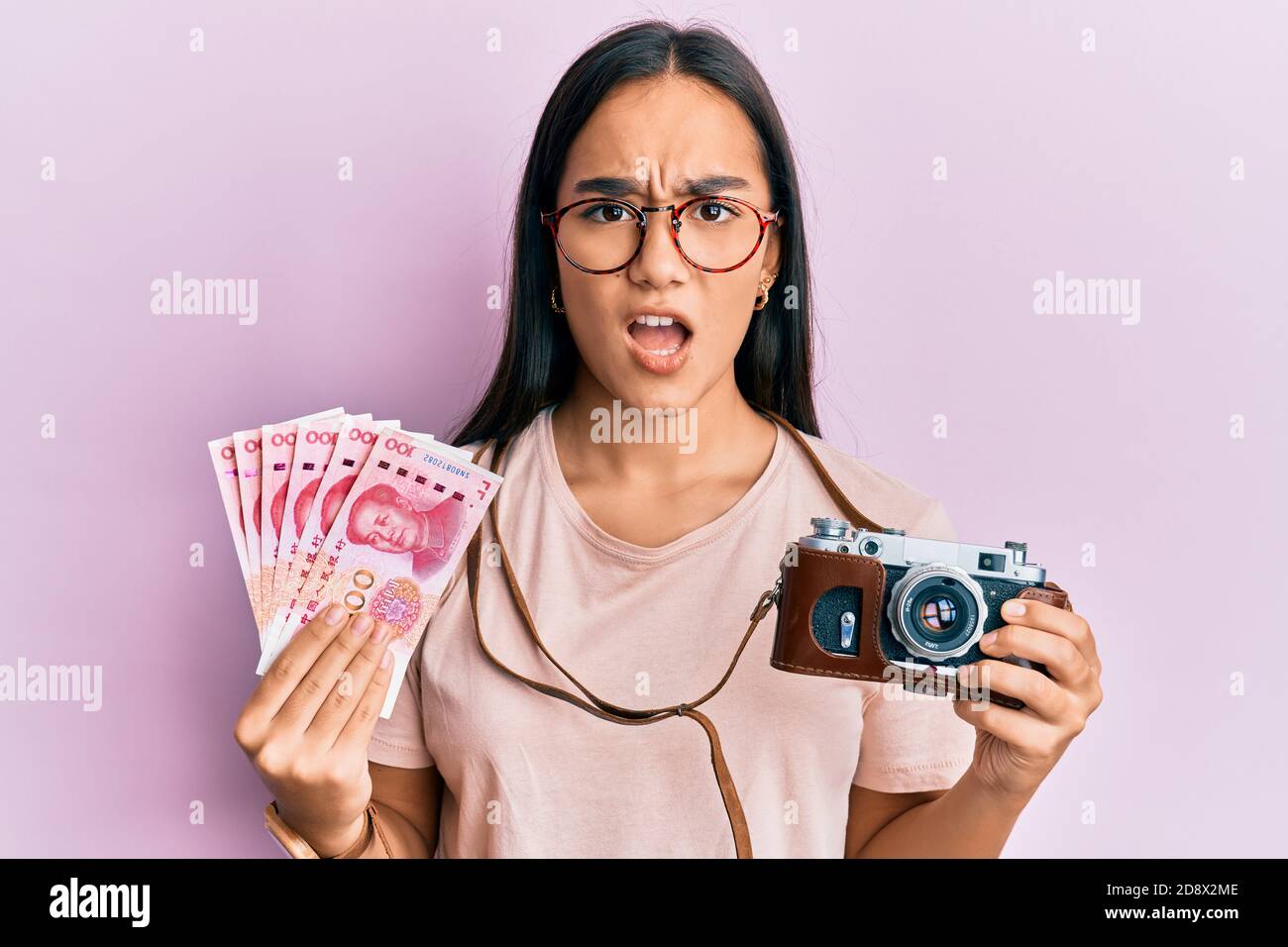 Young asian woman holding vintage camera and 100 chinese yuan clueless ...