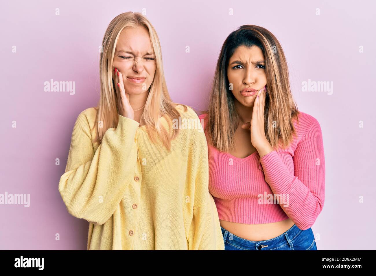 Two friends standing together over pink background touching mouth with ...