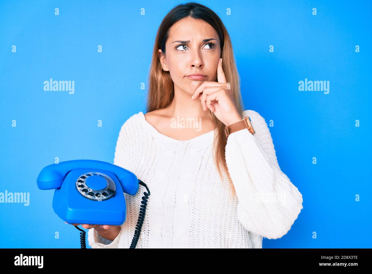 Young brunette woman using vintage telephone serious face thinking ...