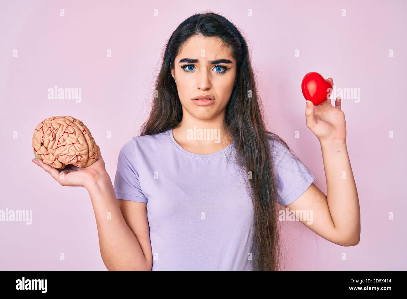 Brunette teenager girl holding brain and heart clueless and confused ...