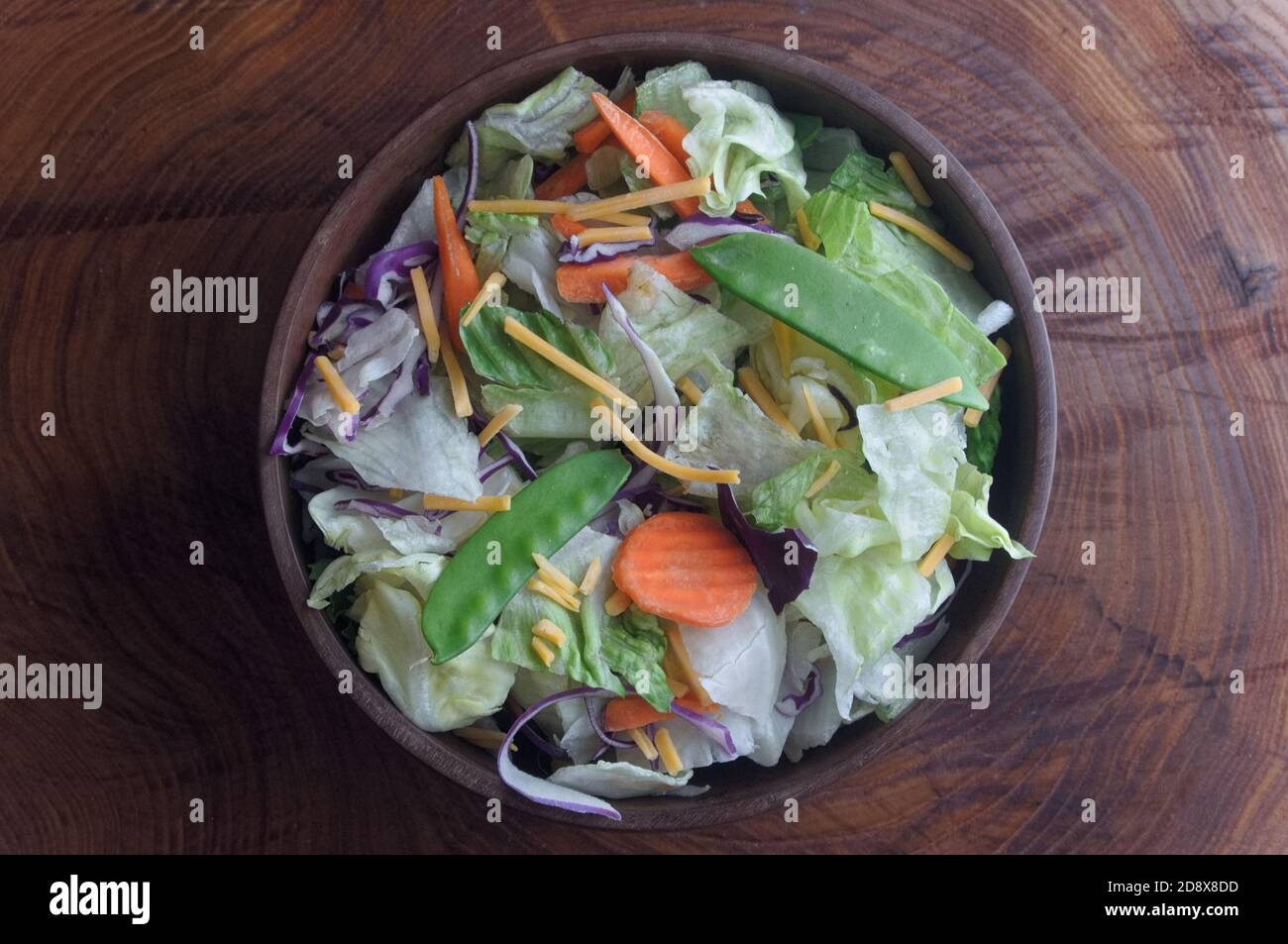A mixed vegetable salad in a round wooden bowl atop a wooden cross ...