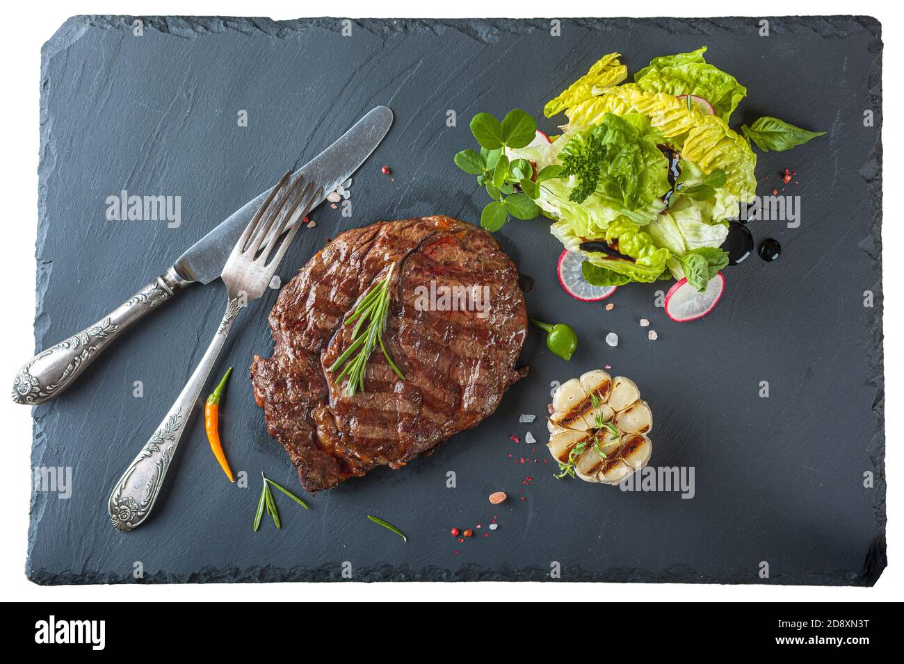 A ribeye steak with sprig of rosemary anh salad on a black stone slab ...