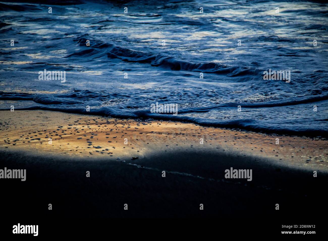 Dramatic dark blue late evening ocean bubbling onto pebbly beach Stock ...