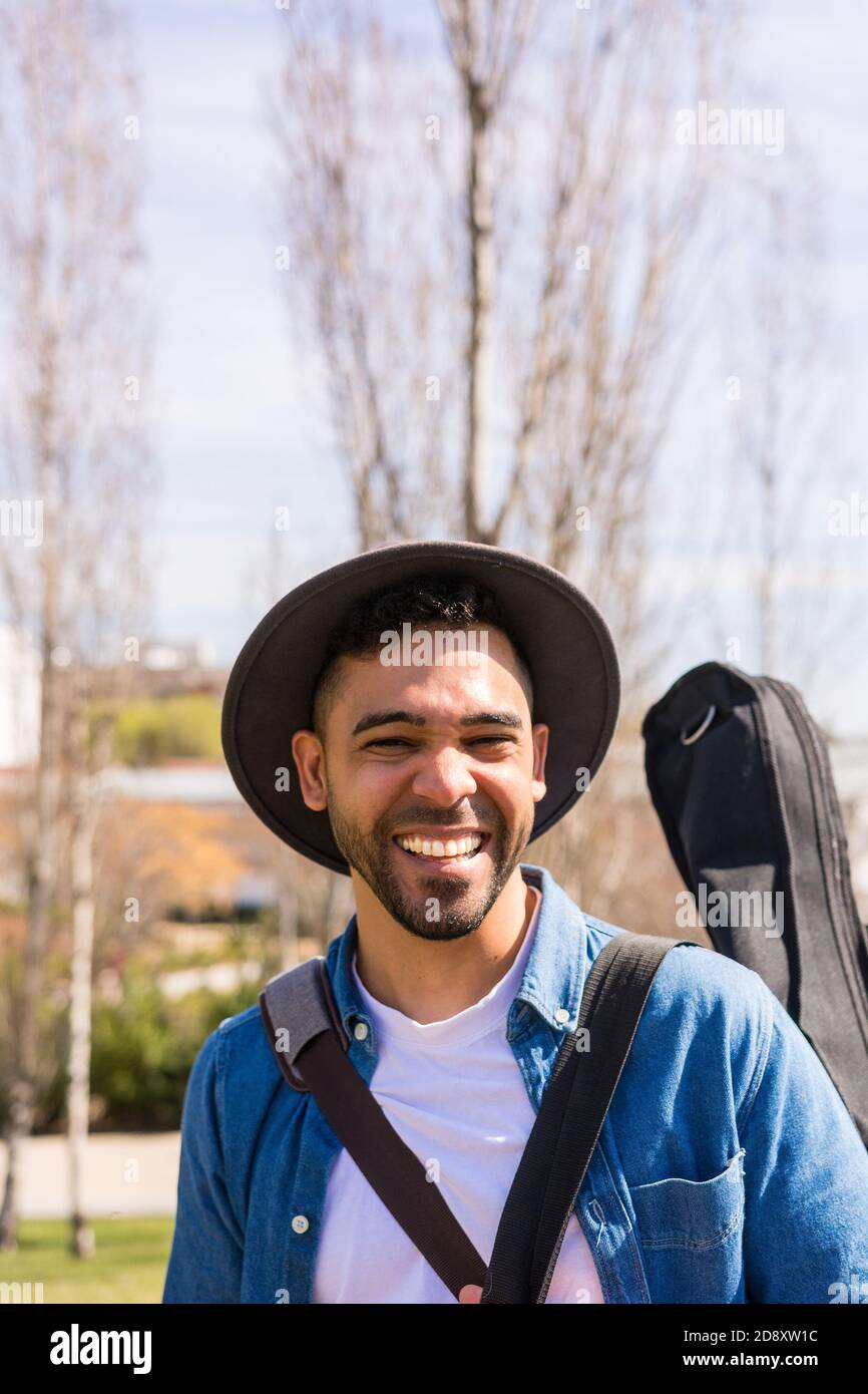 Musician with his guitar on his back and hat smiles because he's happy ...