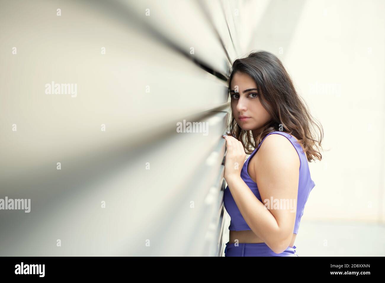 Scared young woman leaning against wall outdoors looking at camera ...