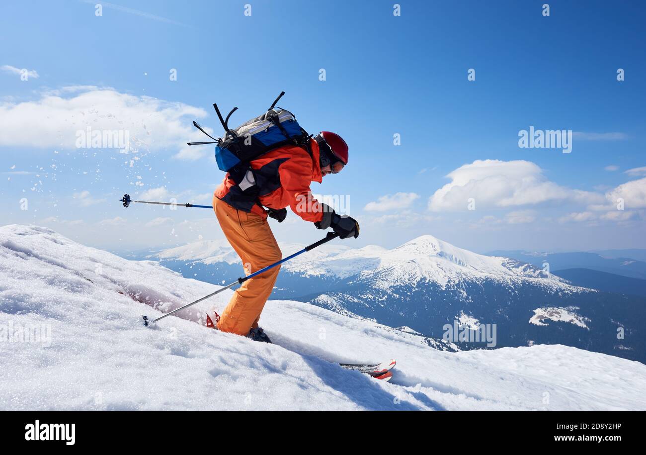Sportsman skier in skiing equipment with backpack riding down steep ...