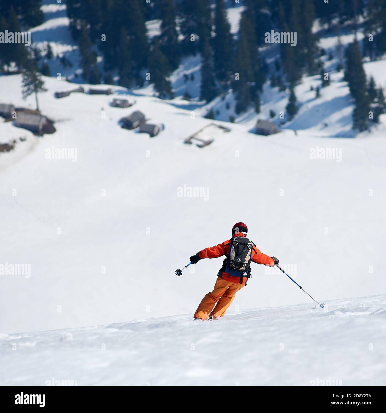 Back view of professional skier in helmet with backpack riding skis in ...