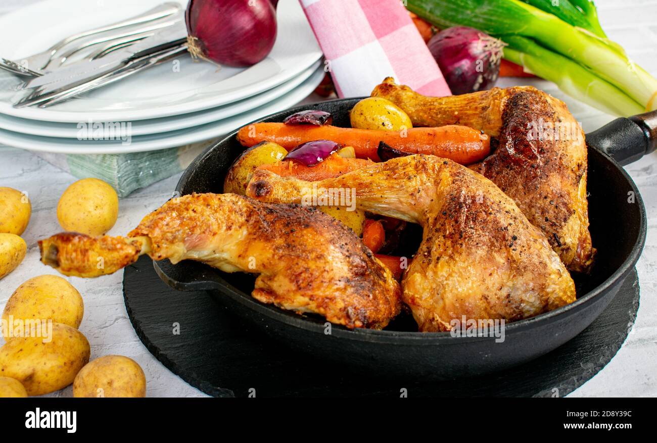 Meal with roasted chicken legs served for dinner in an skillet on a table with plates Stock Photo Alamy