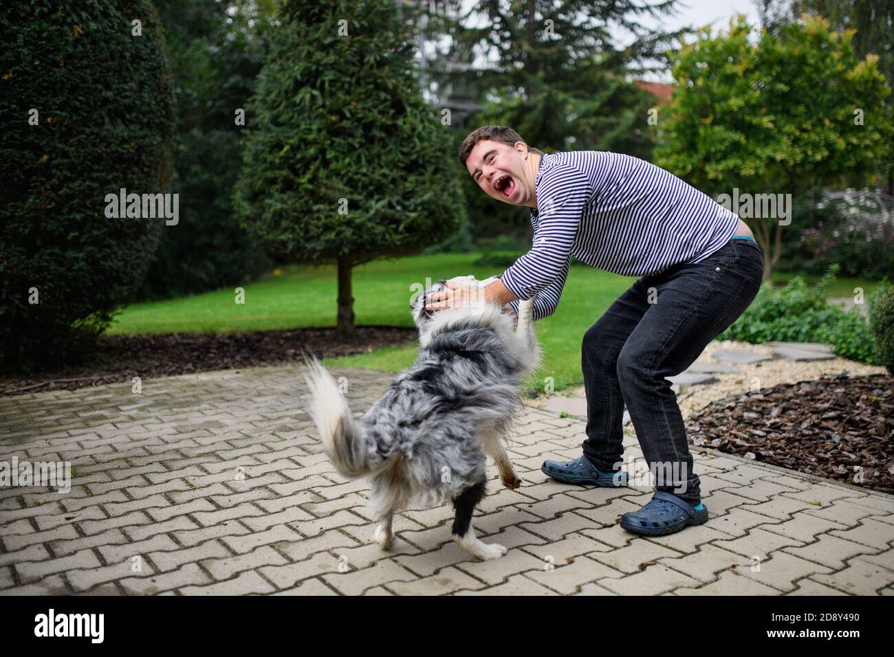 Portrait of cheerful down syndrome adult man playing with dog outdoors ...
