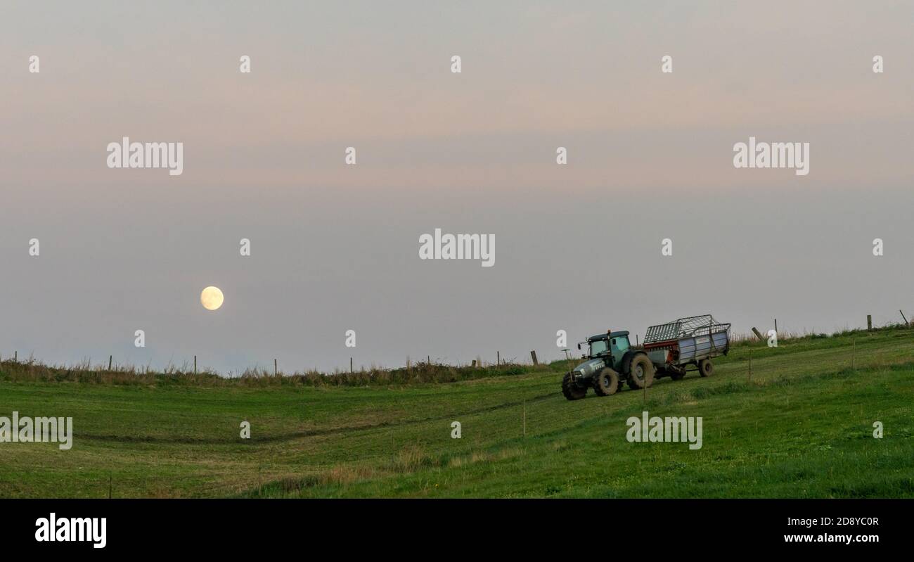 farmer with tractor and trailer cultivating fields under a full moon at ...