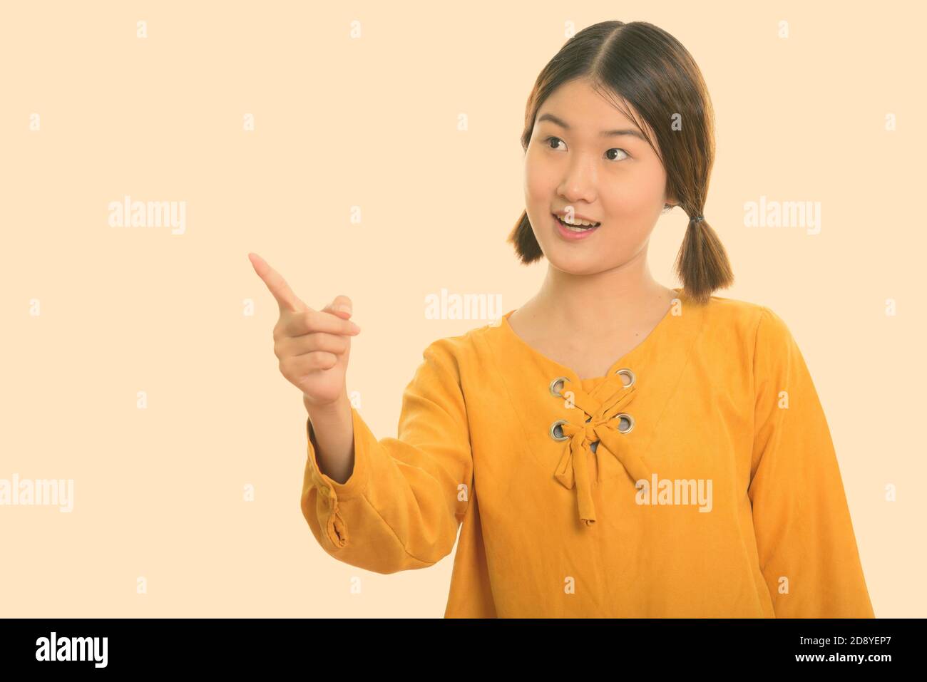 Studio shot of young beautiful Asian woman pointing finger at distance ...