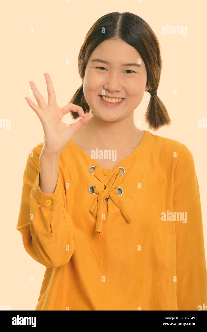 Studio shot of young happy Asian woman smiling while giving ok sign ...