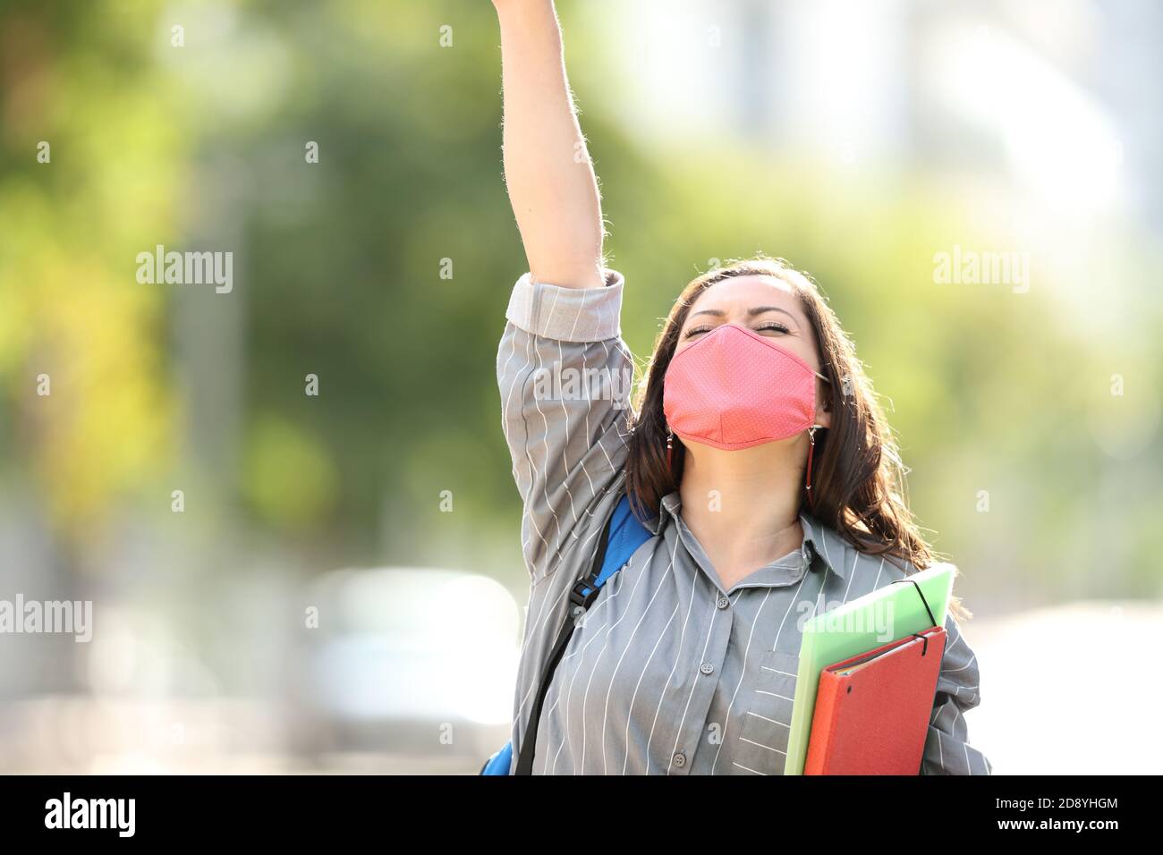 Front view portrait of an excited student wearing mask raising arm in ...