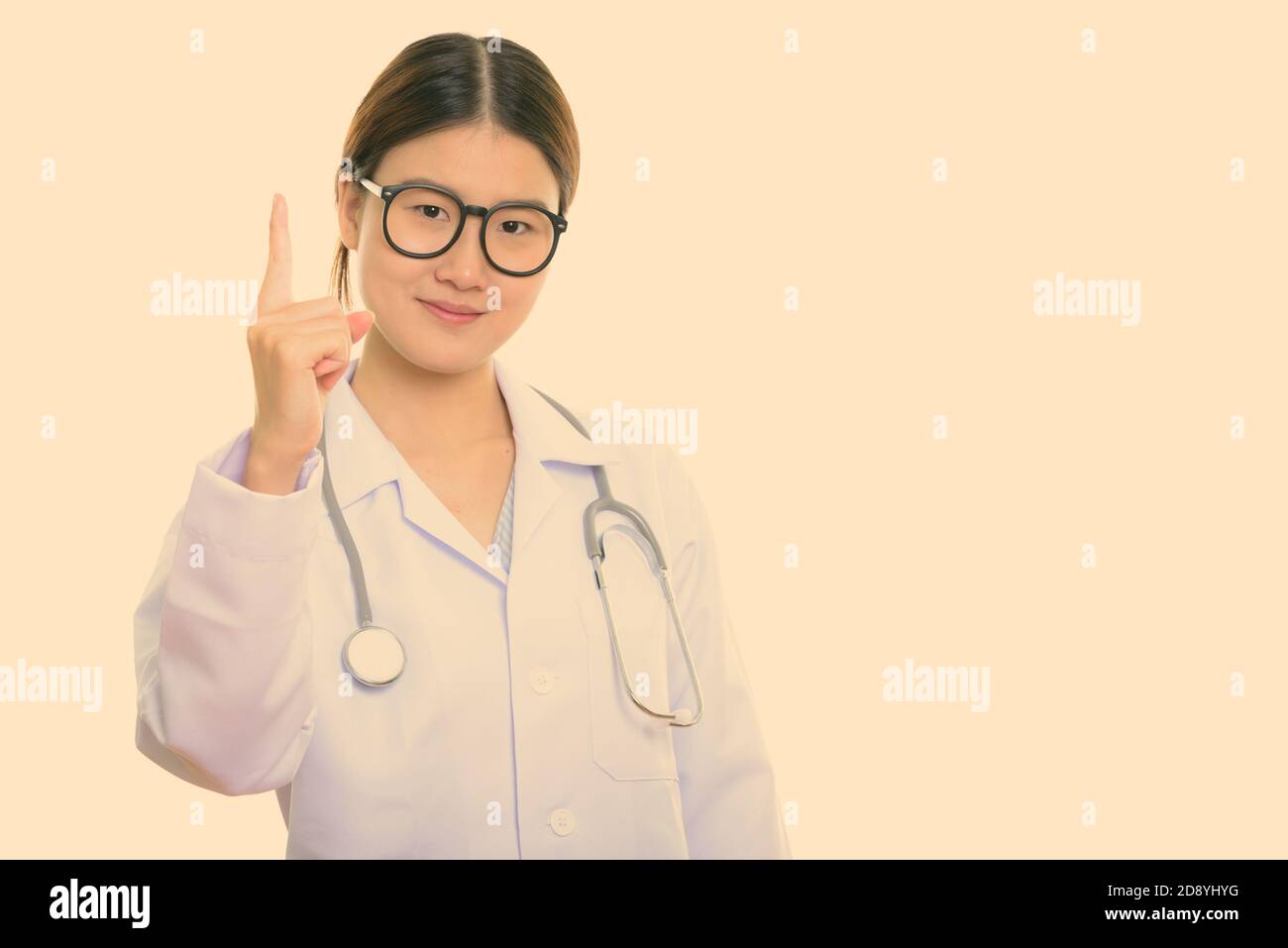 Studio shot of young beautiful Asian woman doctor pointing finger up ...