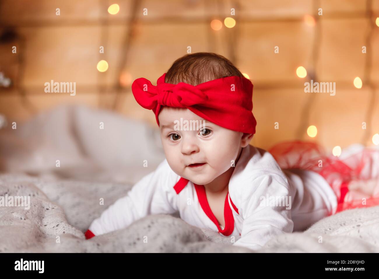 Cute baby girl in red bow on head and white sweater lying on blanket, a ...