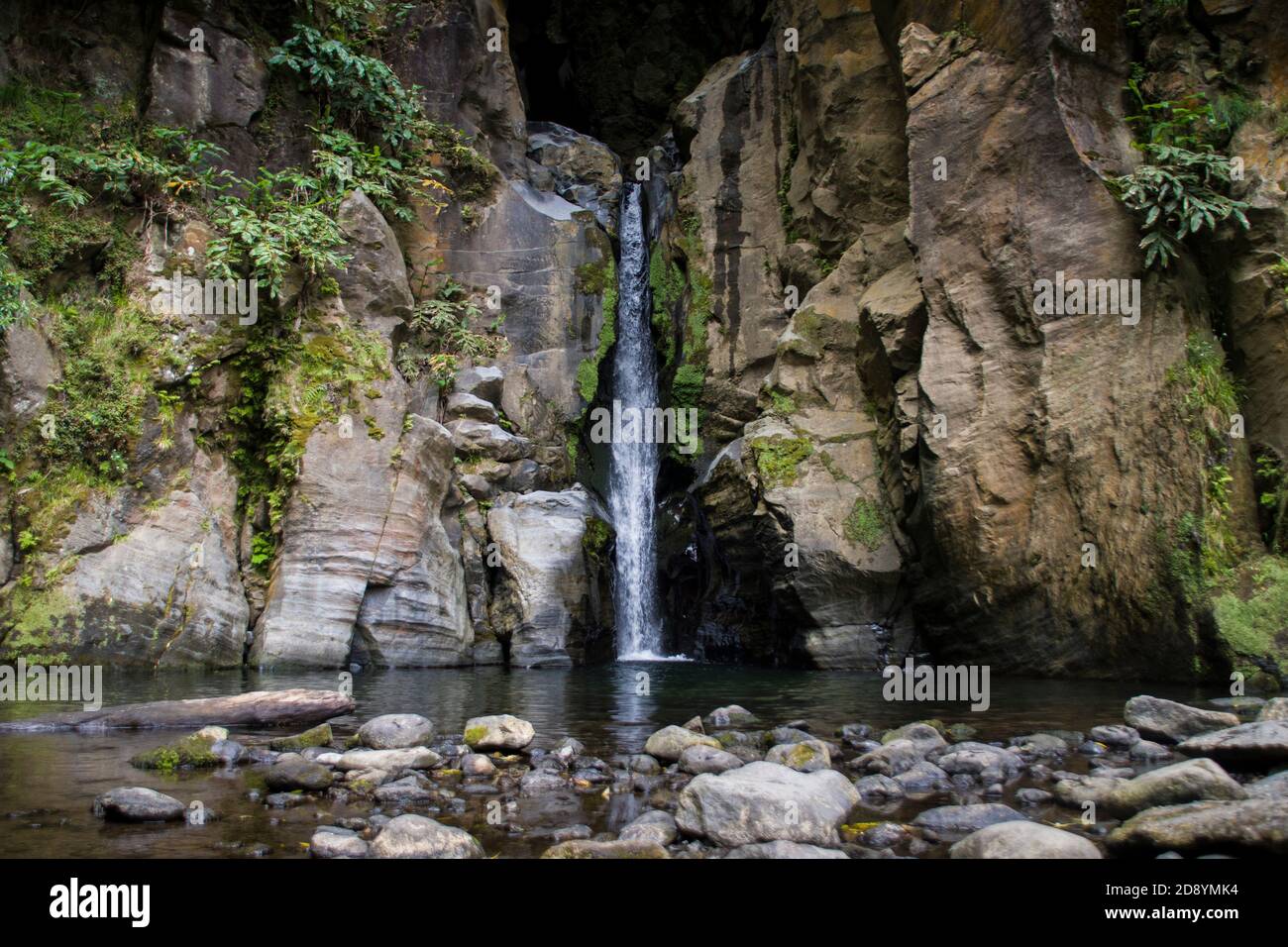 A narrow waterfall falls between rocky stone walls to a lake in the ...