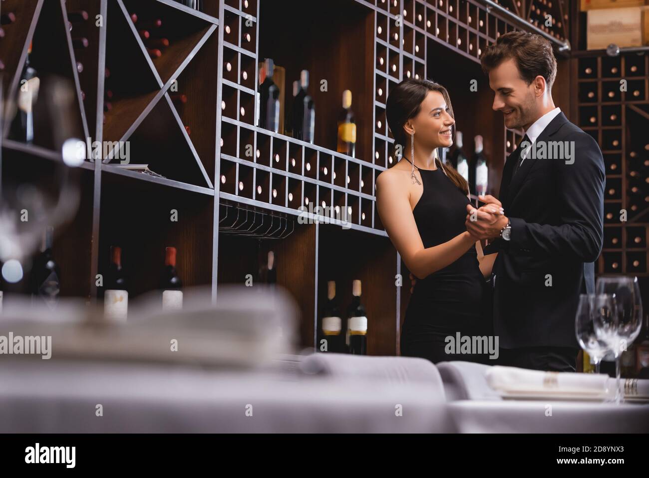 Selective focus of elegant couple dancing near racks with wine bottles ...