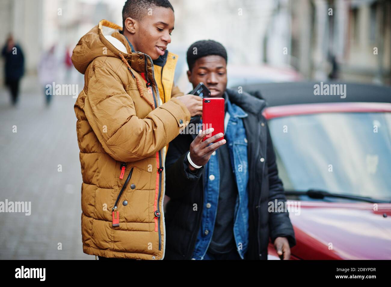 Two african male friends standing near red american convertible car and ...