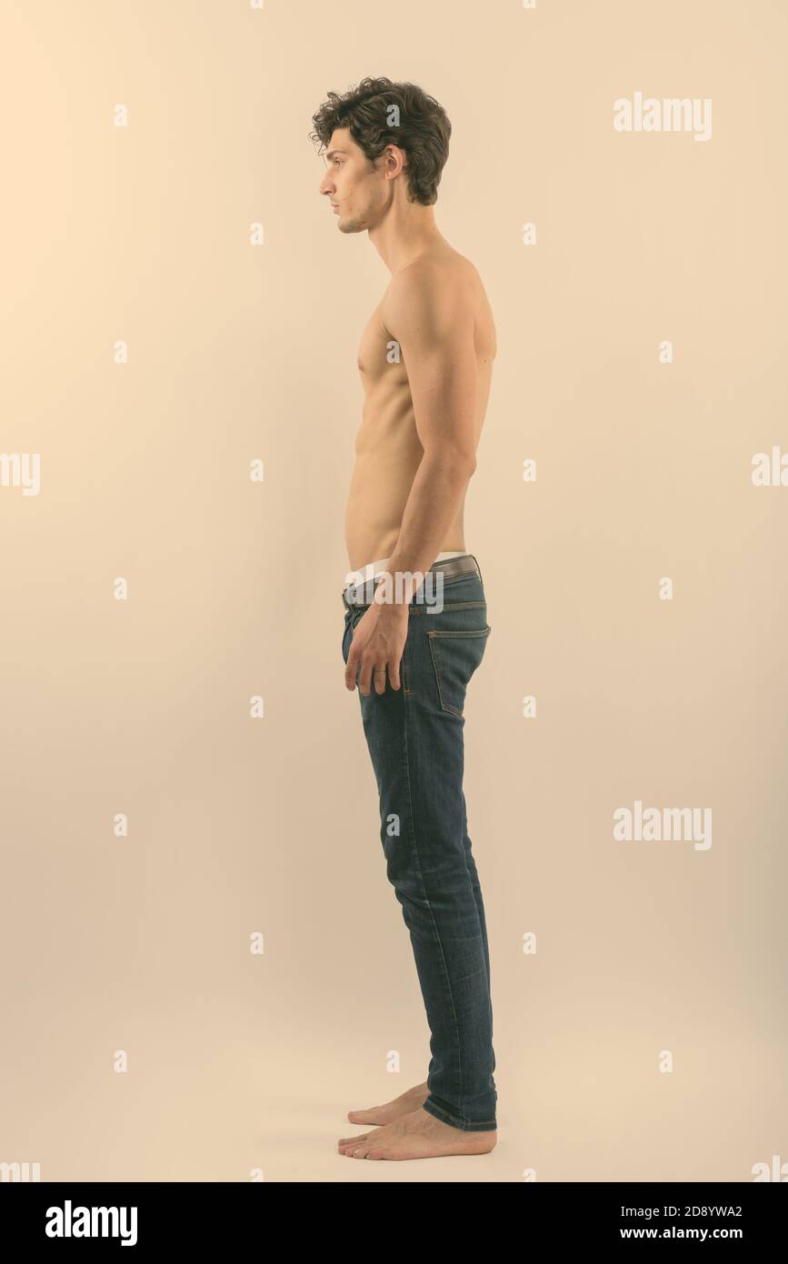 Full body shot of profile view of young handsome man standing shirtless ...