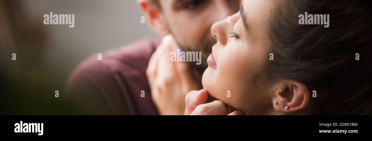 man on blurred background touching face of beloved woman with closed ...