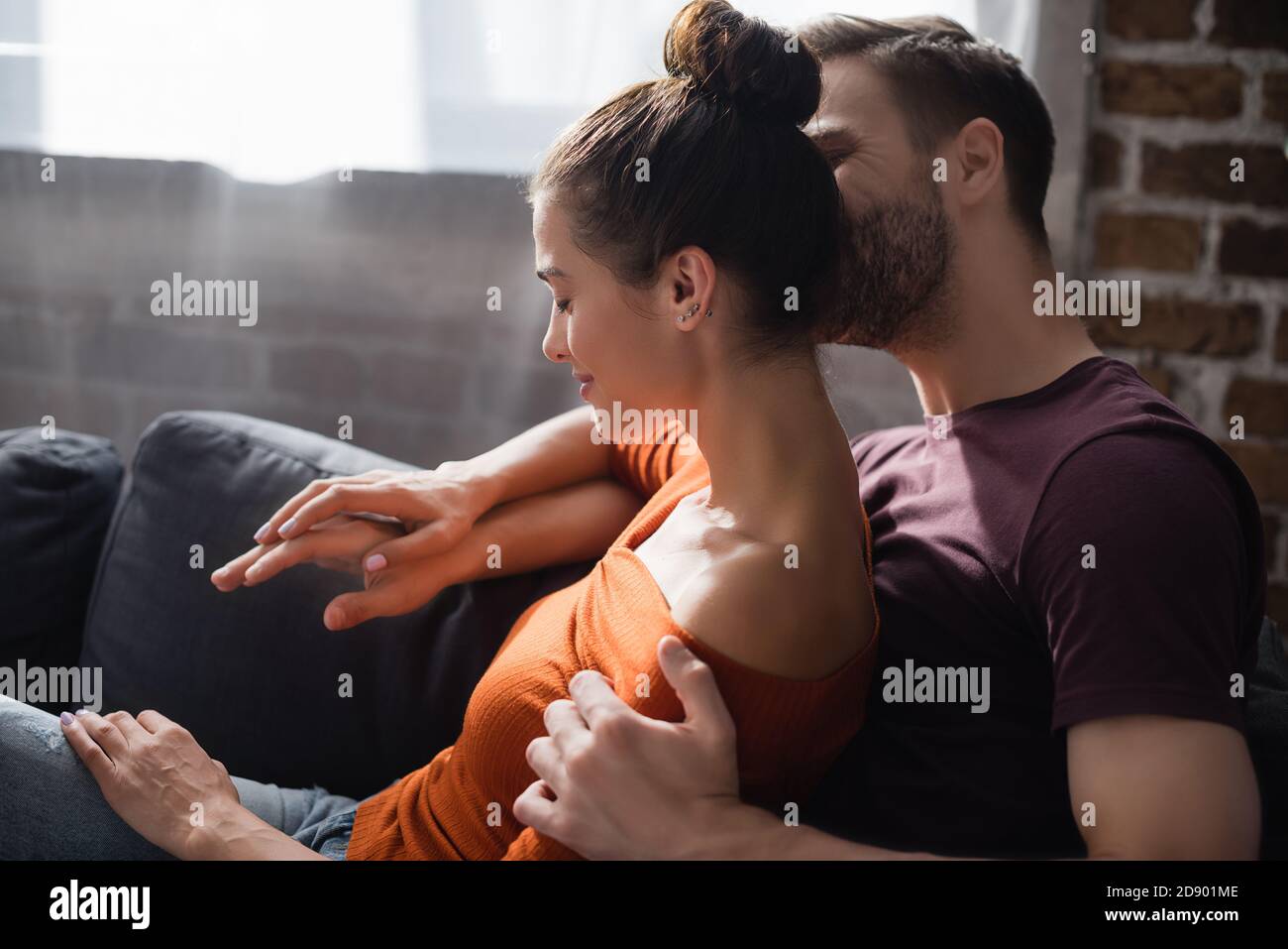 tender man embracing beloved woman while sitting on sofa at home Stock ...