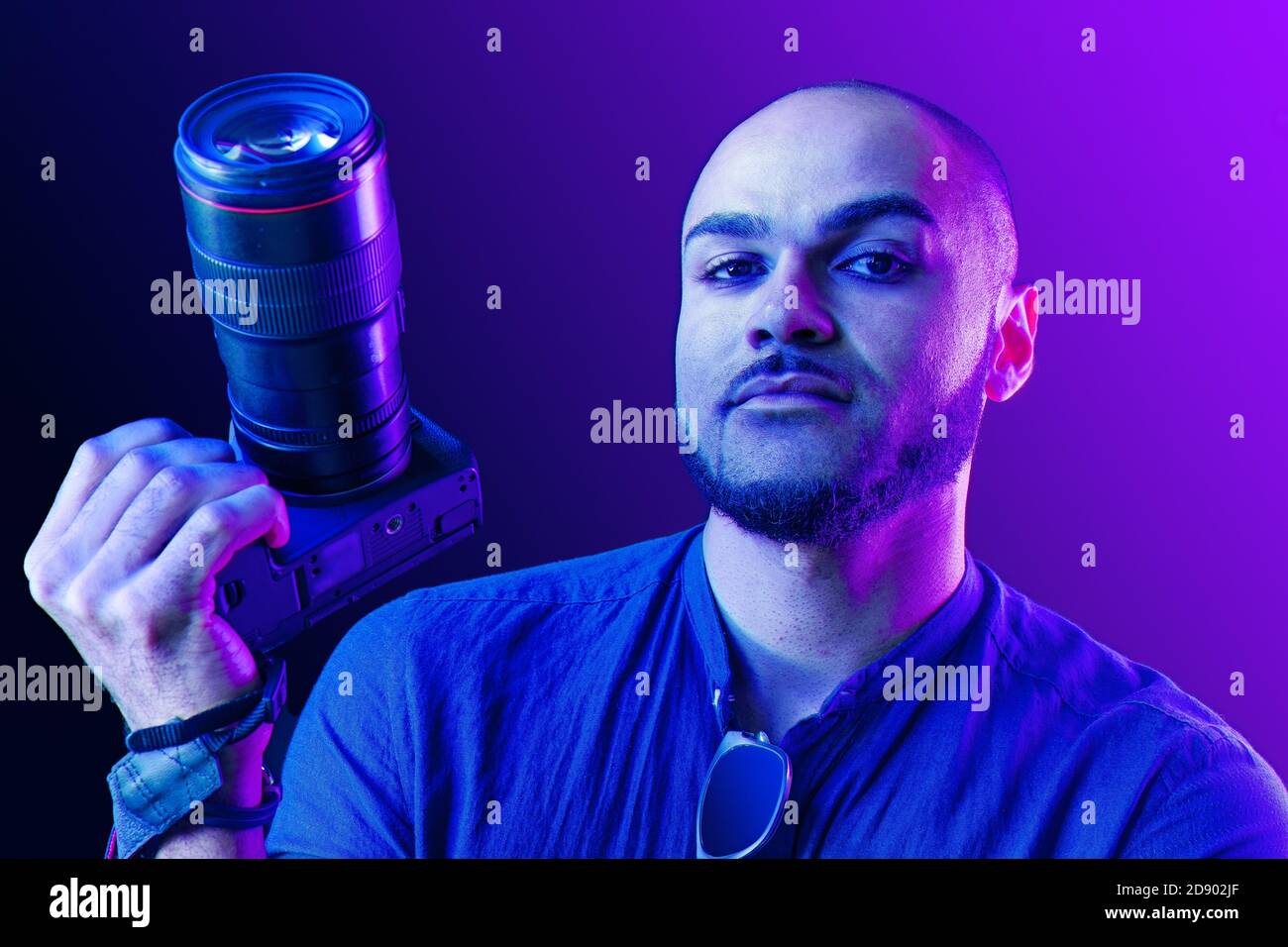 Black man with camera standing against purple background in neon light ...