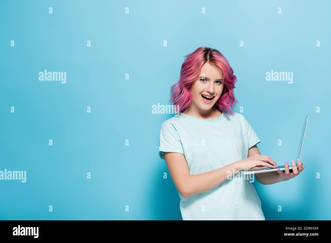 young woman with pink hair using laptop on blue background Stock Photo ...