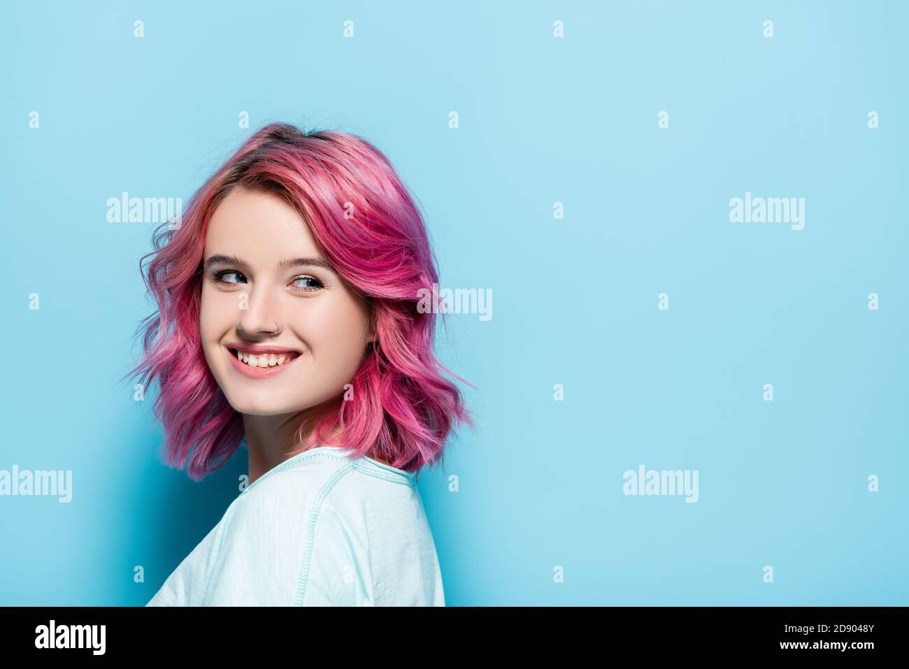 side view of young woman with pink hair smiling on blue background ...