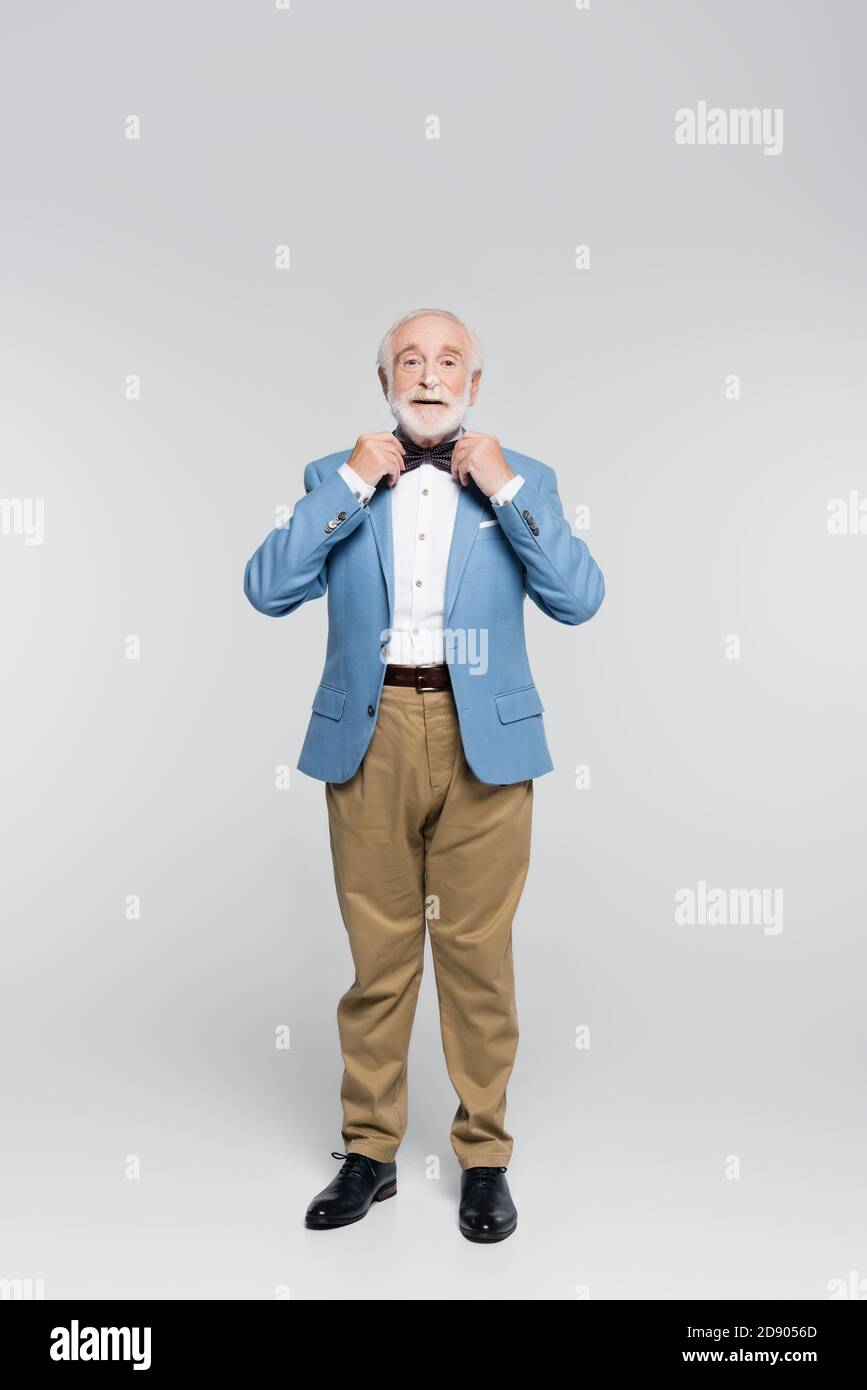 Smiling senior man in jacket adjusting bow tie on grey background Stock ...