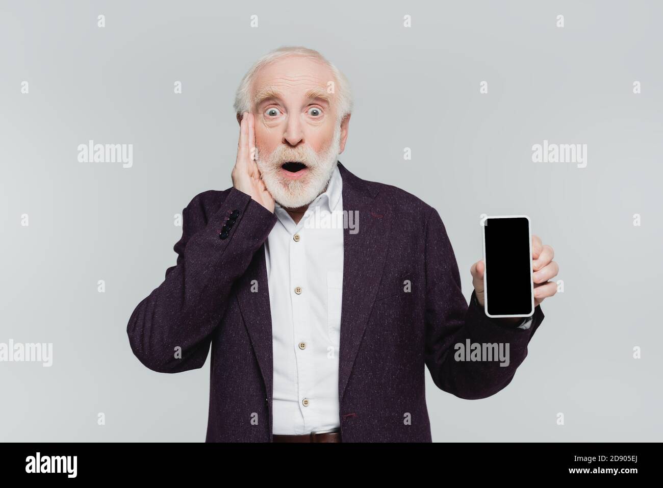 Shocked elderly man looking at camera while holding smartphone with ...