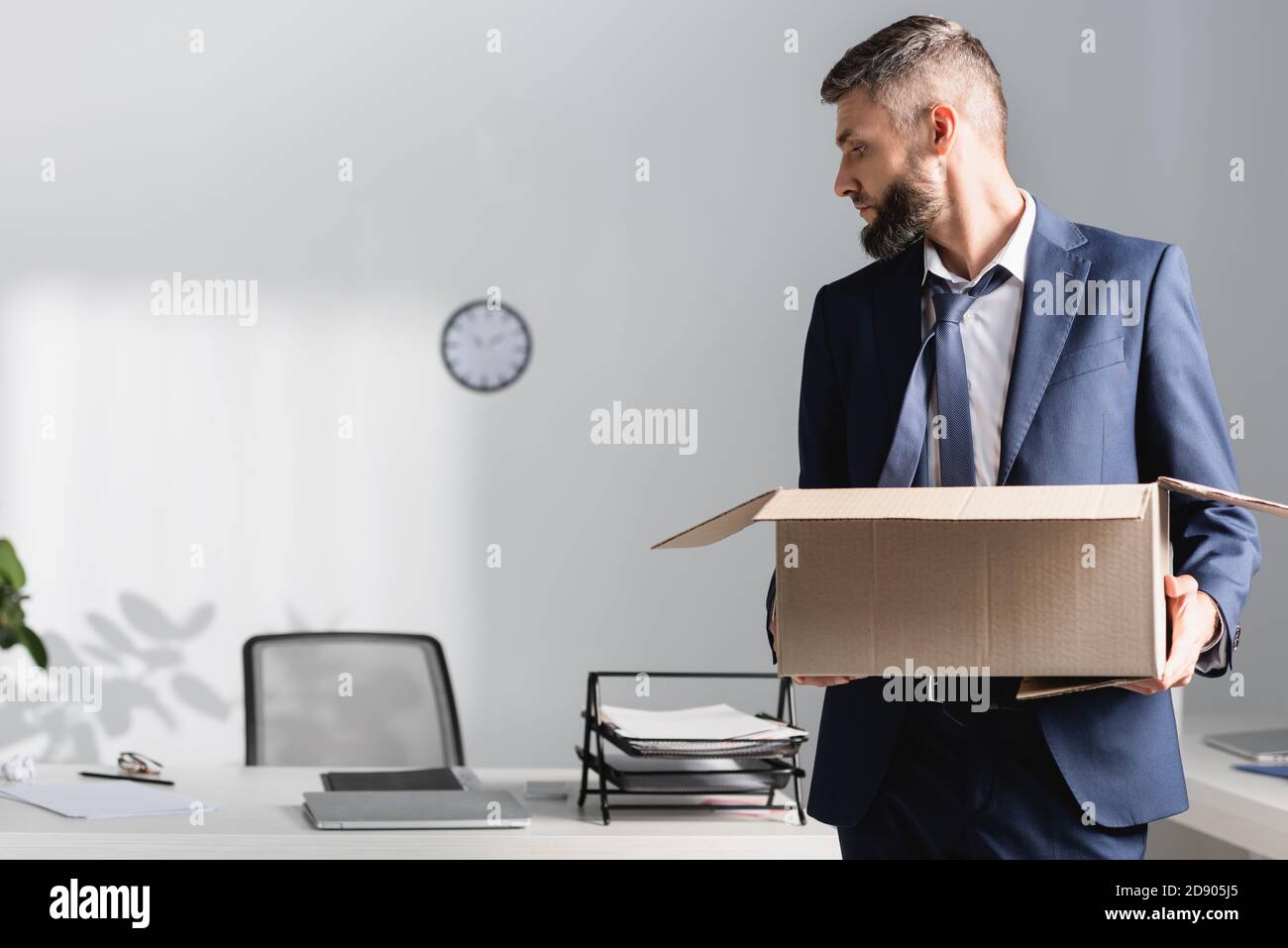 Fired businessman holding carton box near office table on blurred ...