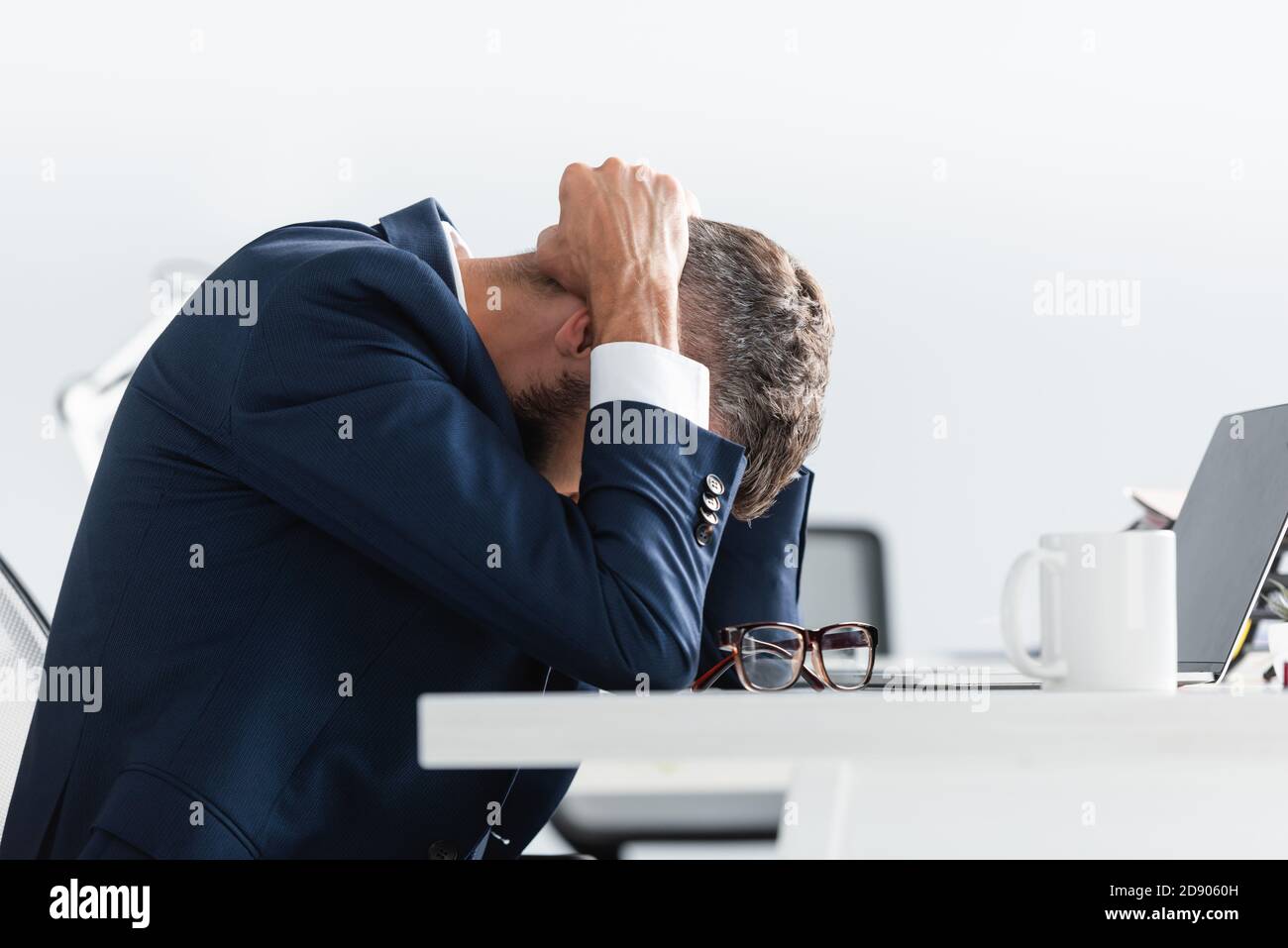 Exhausted businessman in suit touching head while working near laptop ...